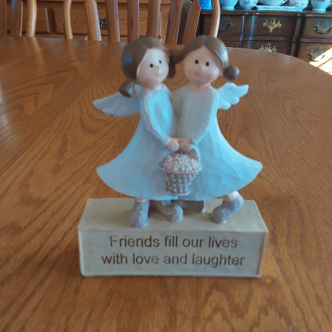 A Figurine of 2 Hugging Friend Angels With the Caption Below That Reads ...