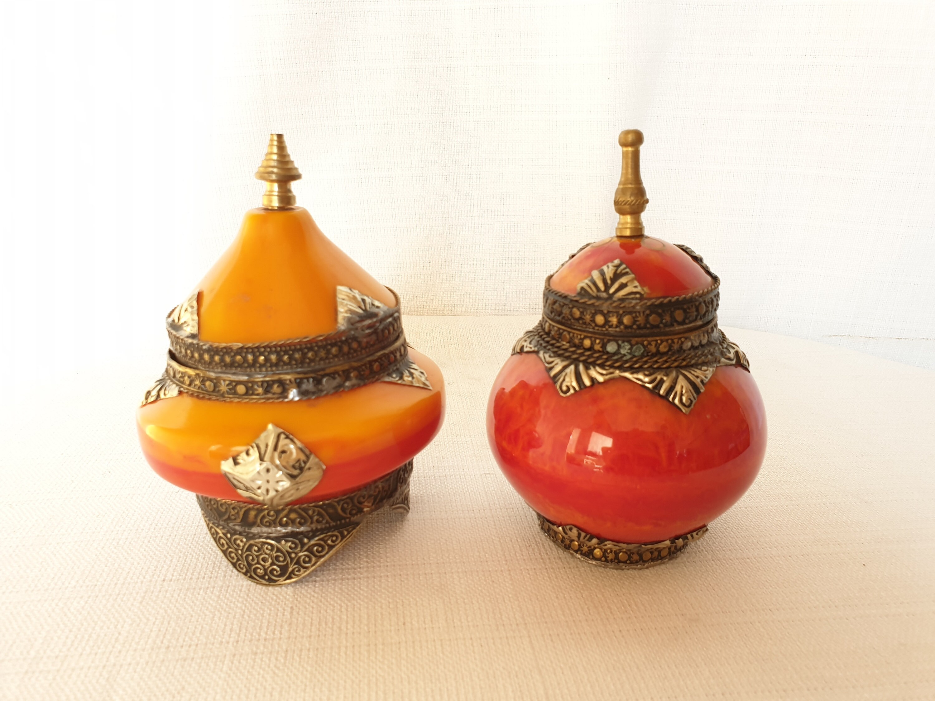 Two ornate orange lid jars, finished with brass ornaments.