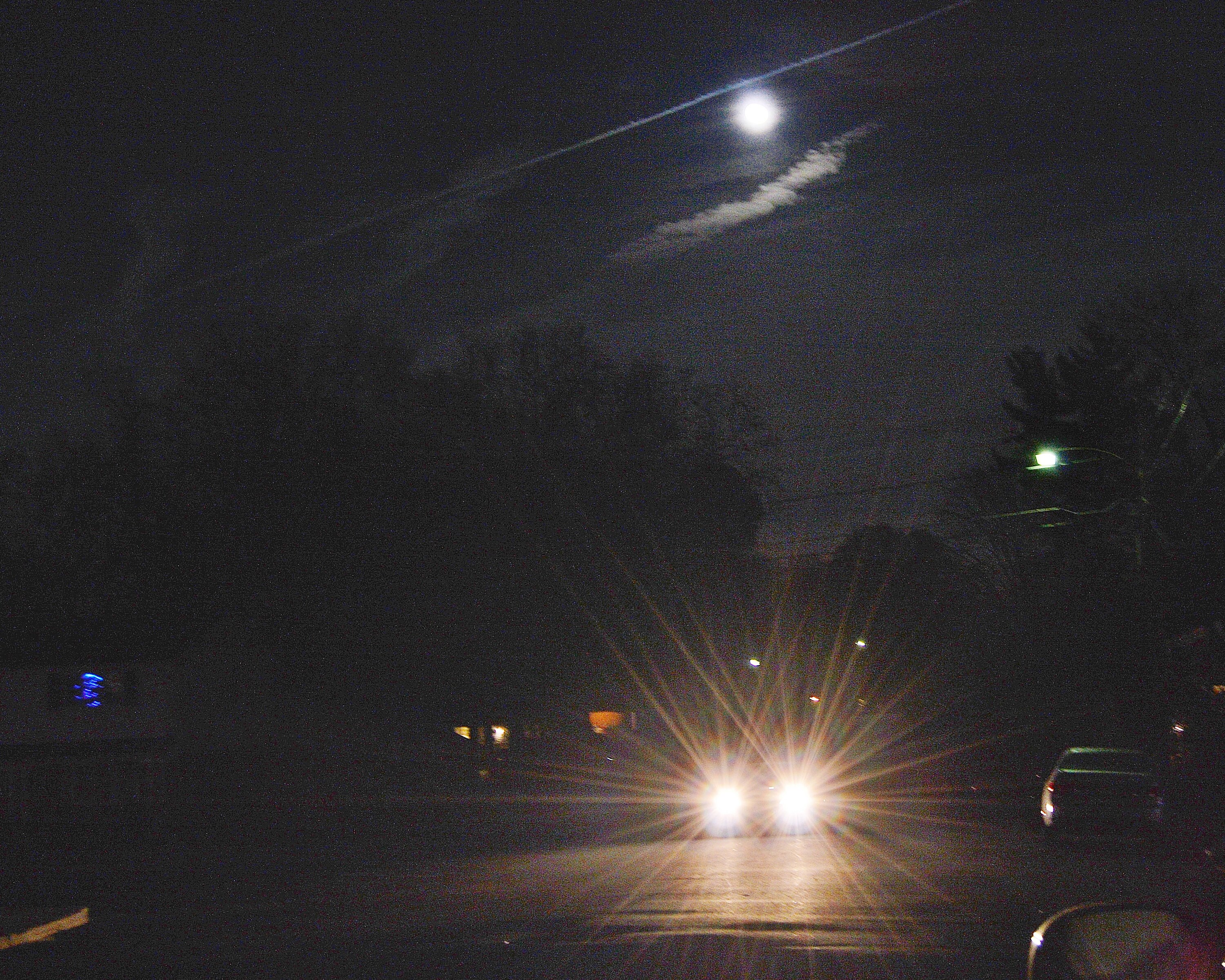 Night View of Car With Bright Headlights Driving Down Street With ...