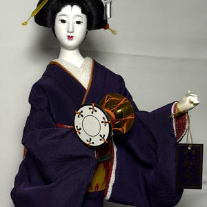 A Beautiful and Cute Geisha Doll. She is Wearing a Purple Kimono With ...
