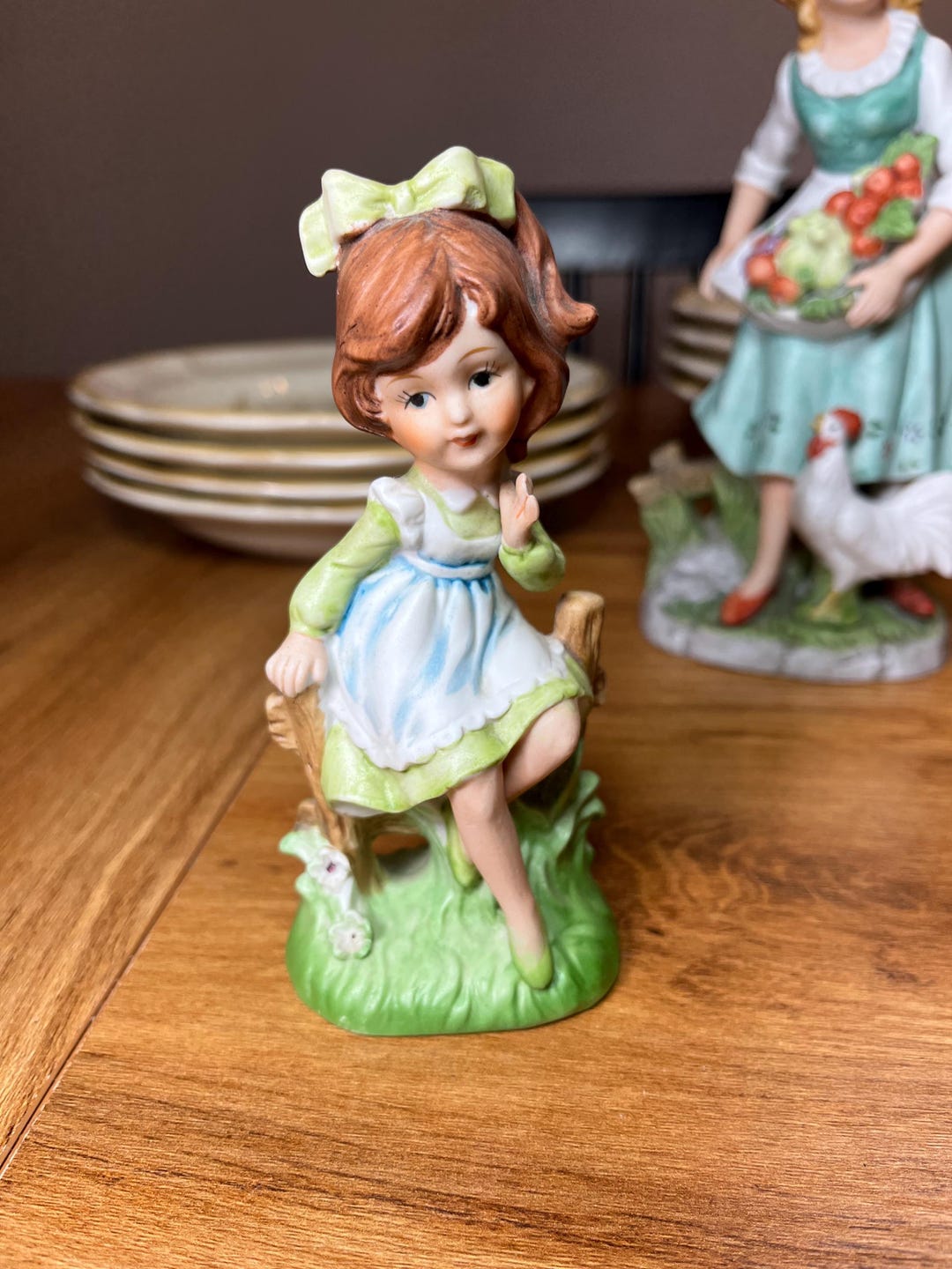 5 Porcelain Figure of Girl Sitting on Fence. She is Wearing a Green ...
